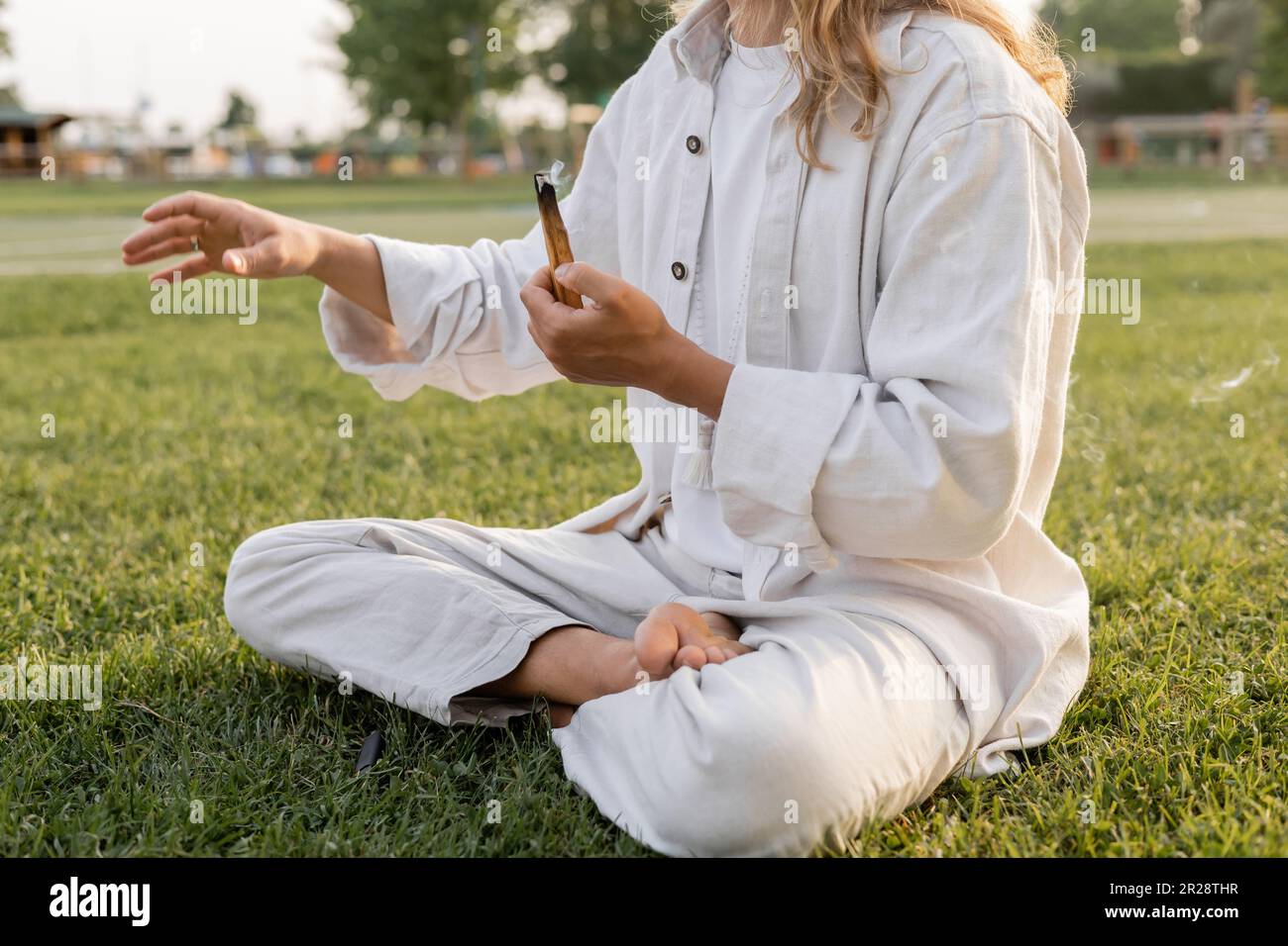 partial view of man in white clothes holding smoldering palo santo ...