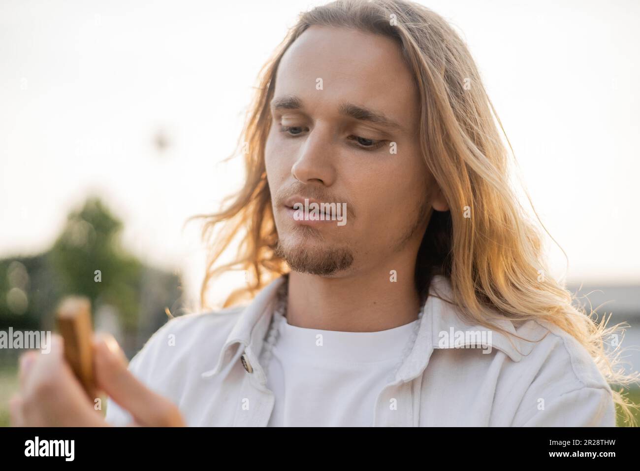 portrait of young man with long fair hair holding blurred palo santo ...