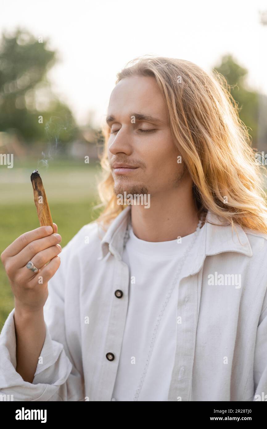 smiling man with long hair and closed eyes enjoying flavor of ...