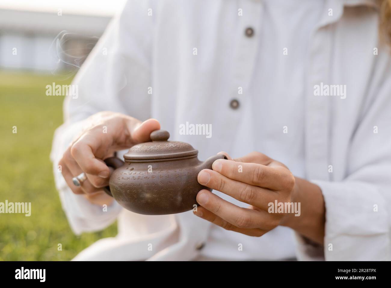 partial view of man in white cotton clothes holding oriental teapot ...