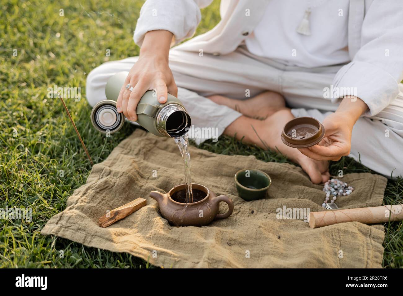 partial view of yoga man pouring hot water in clay teapot while sitting ...