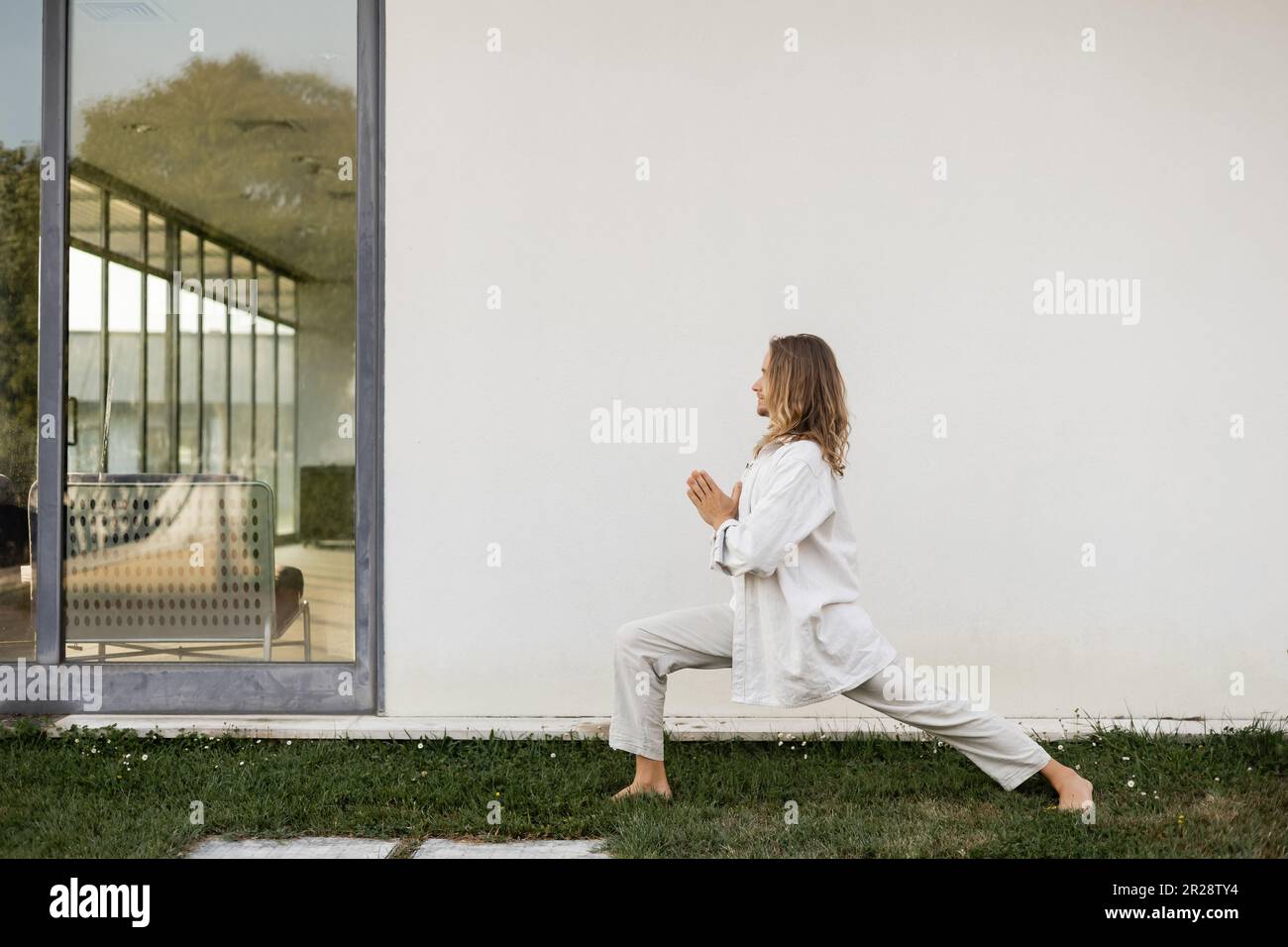 side view of long haired man in linen clothes meditating in warrior ...