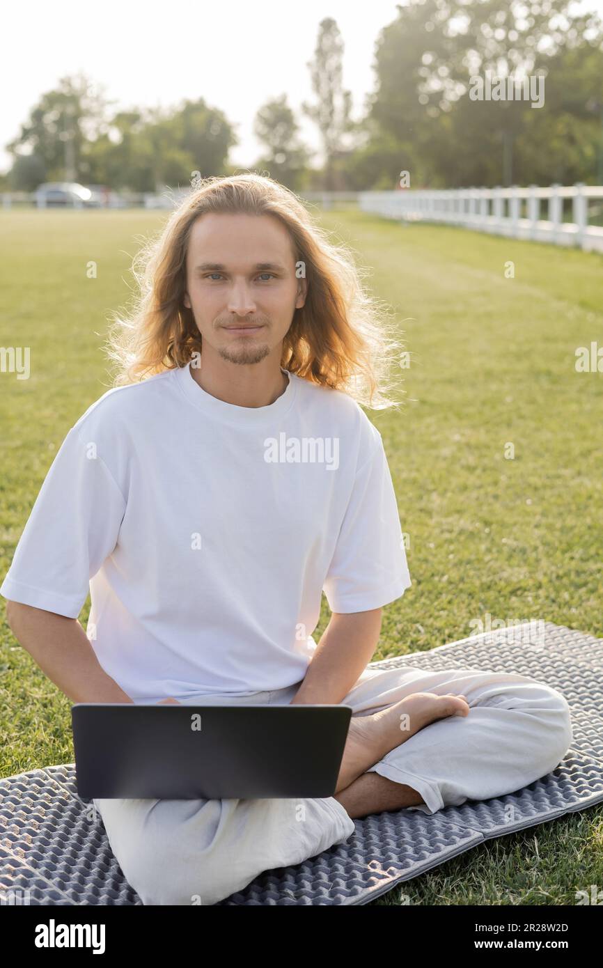 positive long haired yoga man sitting in easy pose near laptop and ...