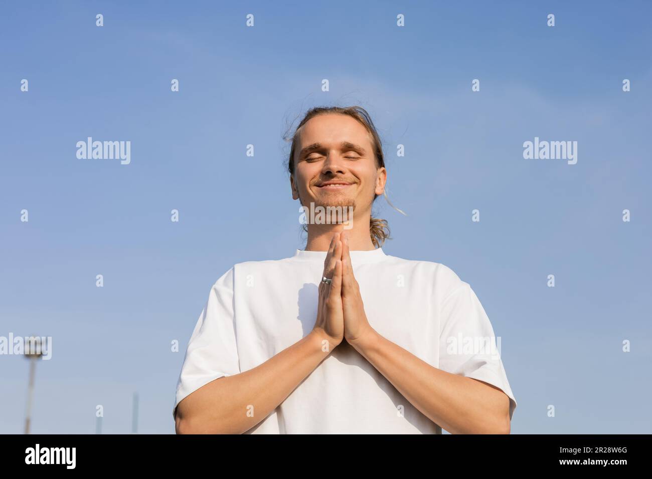 pleased man in white cotton t-shirt meditating with closed eyes and ...