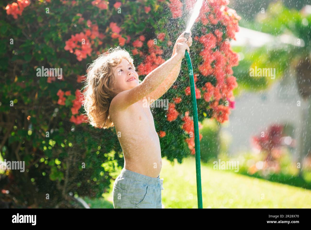 Funny kid playing with garden hose in backyard. Child having fun with ...