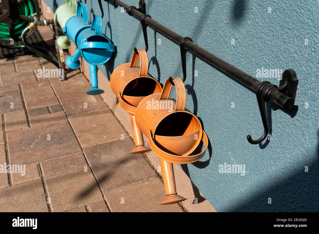 Five coloured metal watering cans for children hanging against wall ...