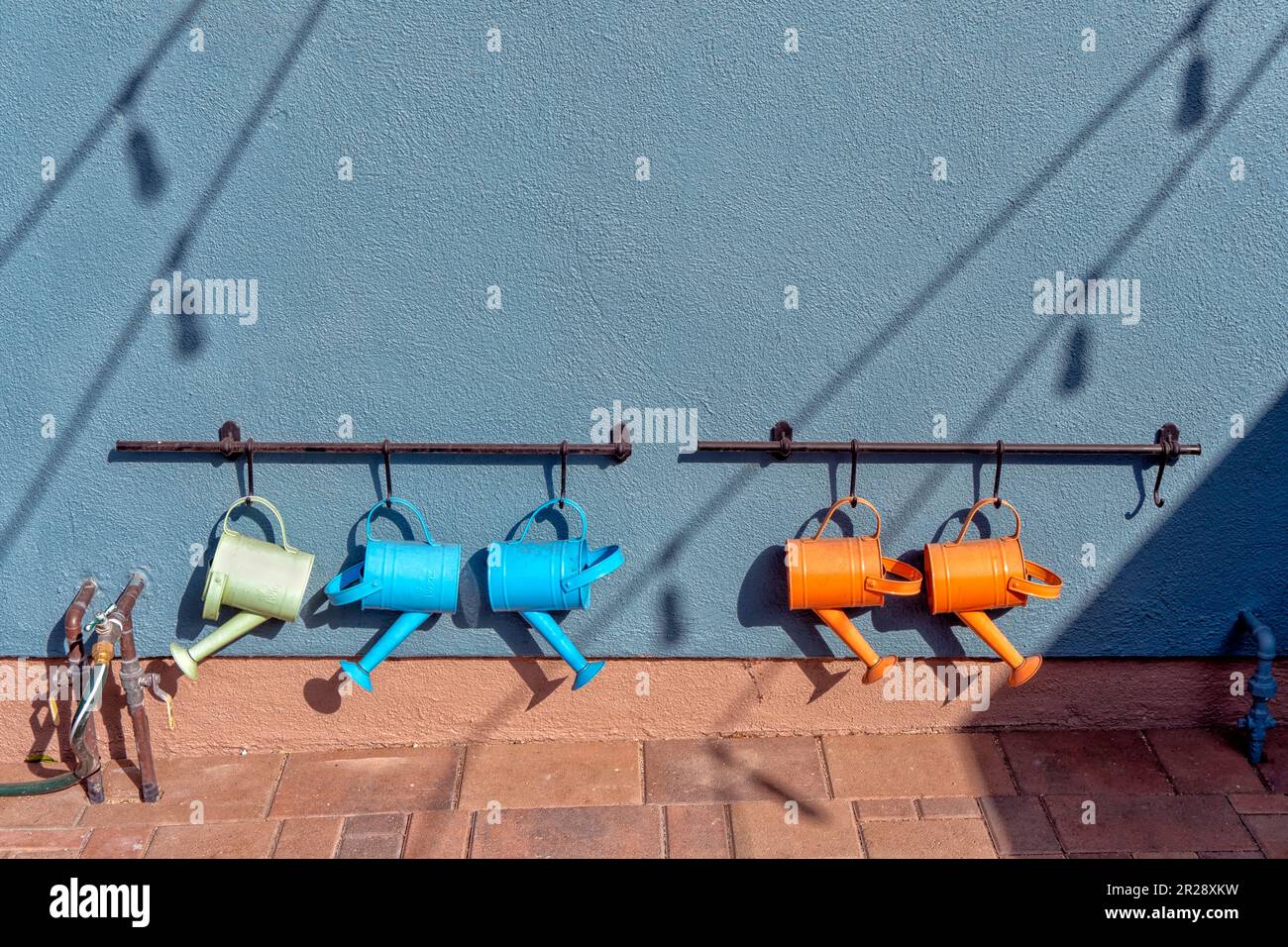 Five coloured metal watering cans for children hanging against wall ...