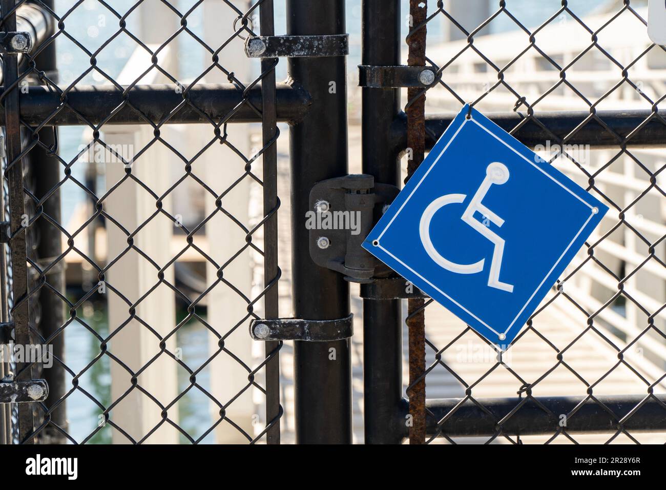 A black chain link metal fence gate with a fallen handicap sign Stock ...
