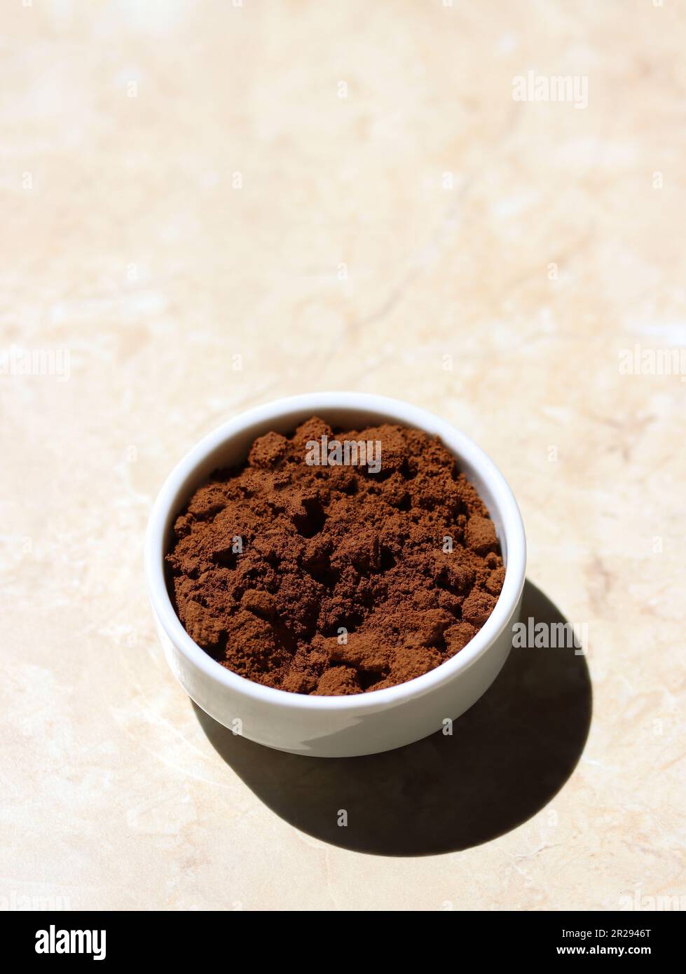 Roasted ground coffee in a small ceramic white bowl on a light marble ...