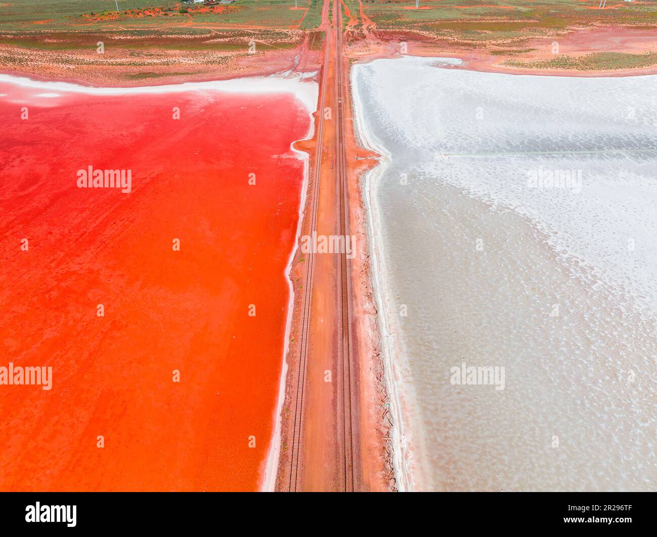 Aerial view of a railway line through a salt lake with vivid red water ...