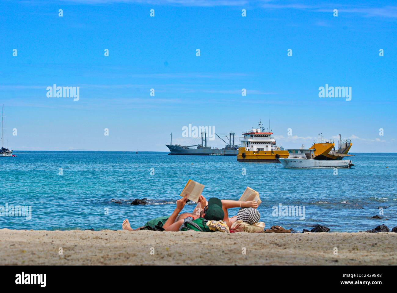 A couple reading at Playa Mann beach. Ships in background. San ...
