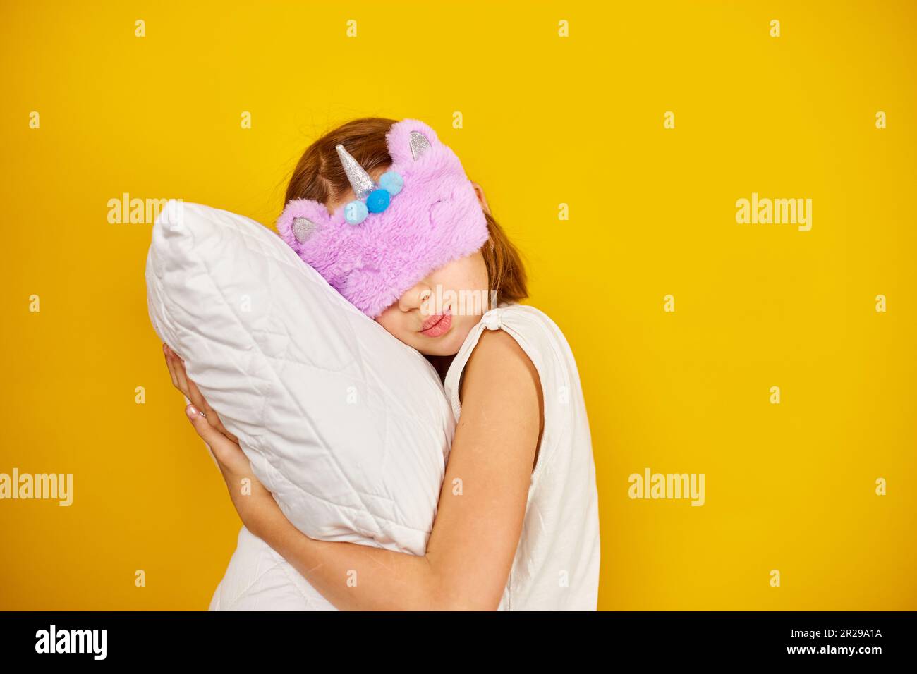 Nice teenage girl in white pyjamas with a violet sleeping mask embraces ...