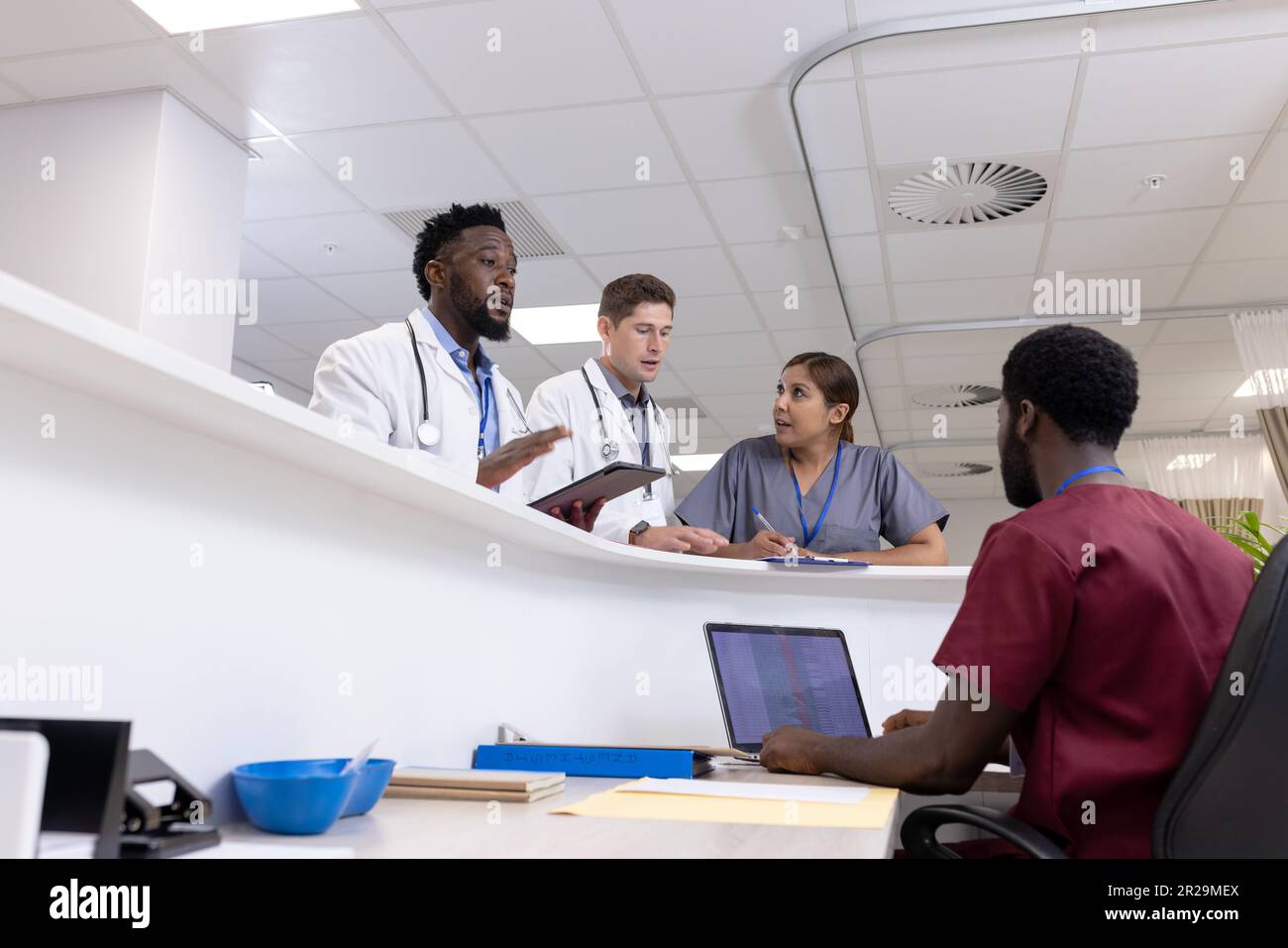 Busy diverse doctors and medical staff talking at reception desk of ...