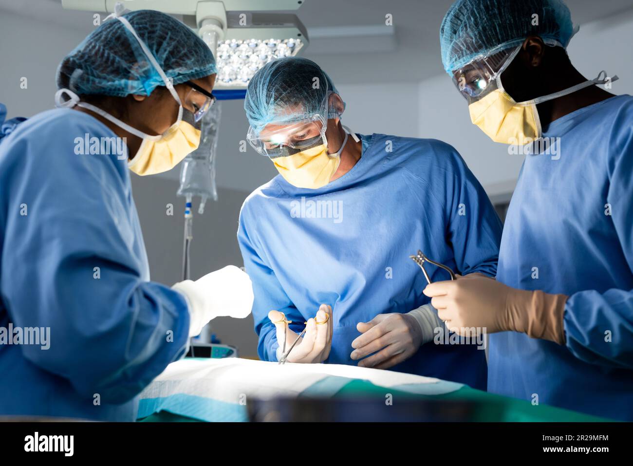 Diverse group of surgeons operating on patient in operating theatre ...