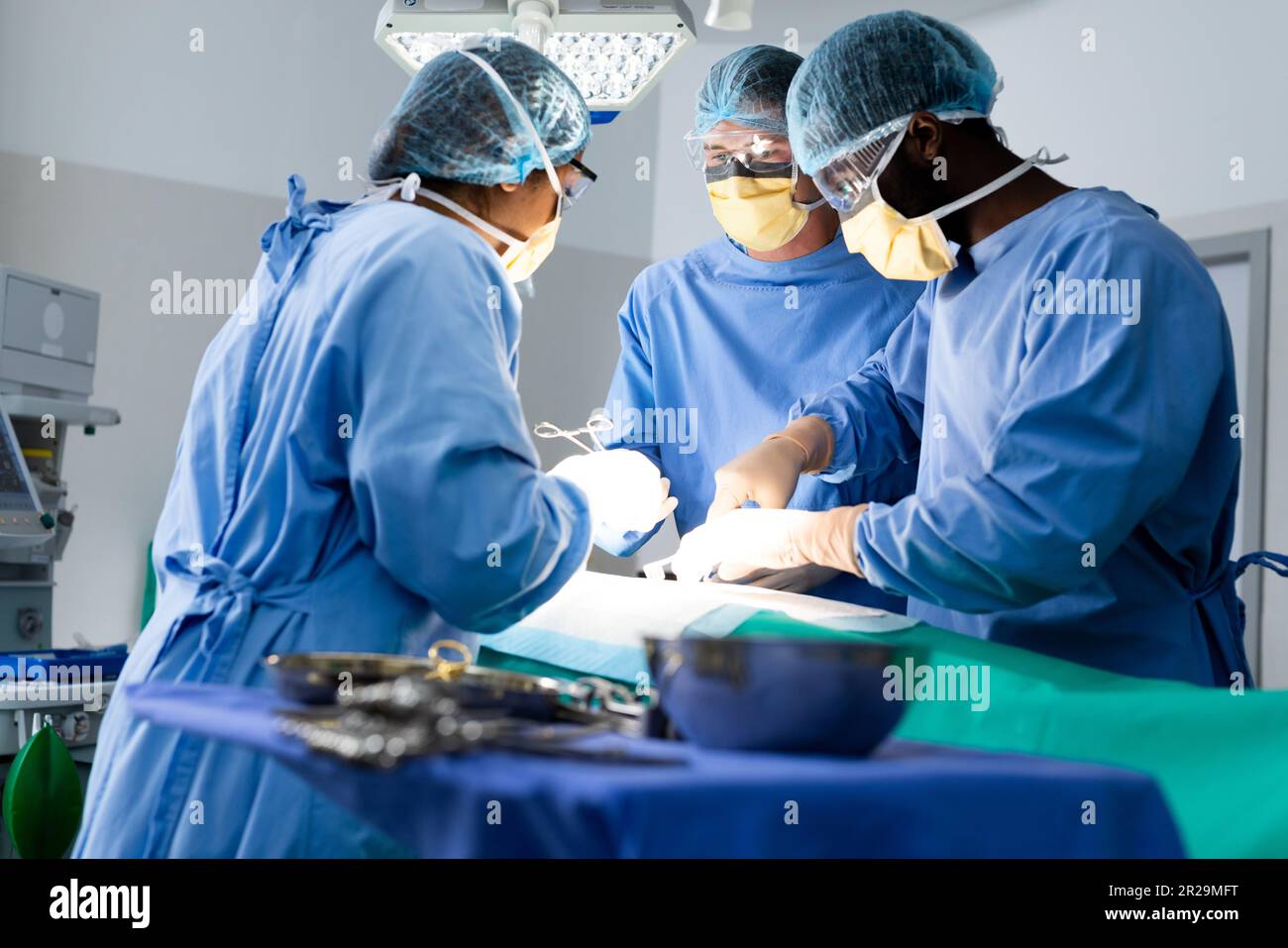 Diverse group of surgeons operating on patient in operating theatre ...