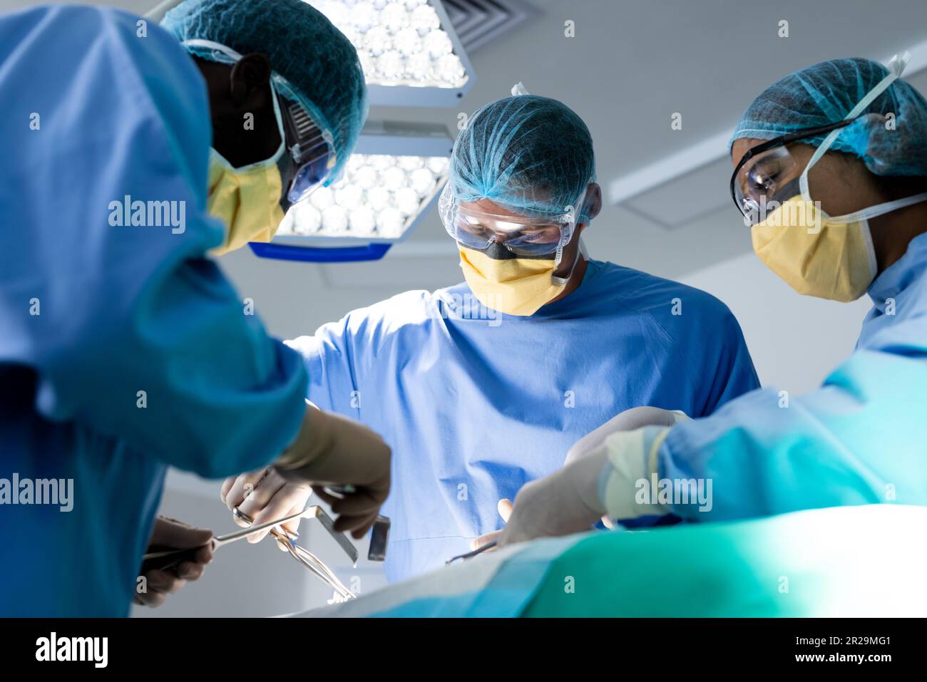 Diverse group of surgeons operating on patient in operating theatre ...
