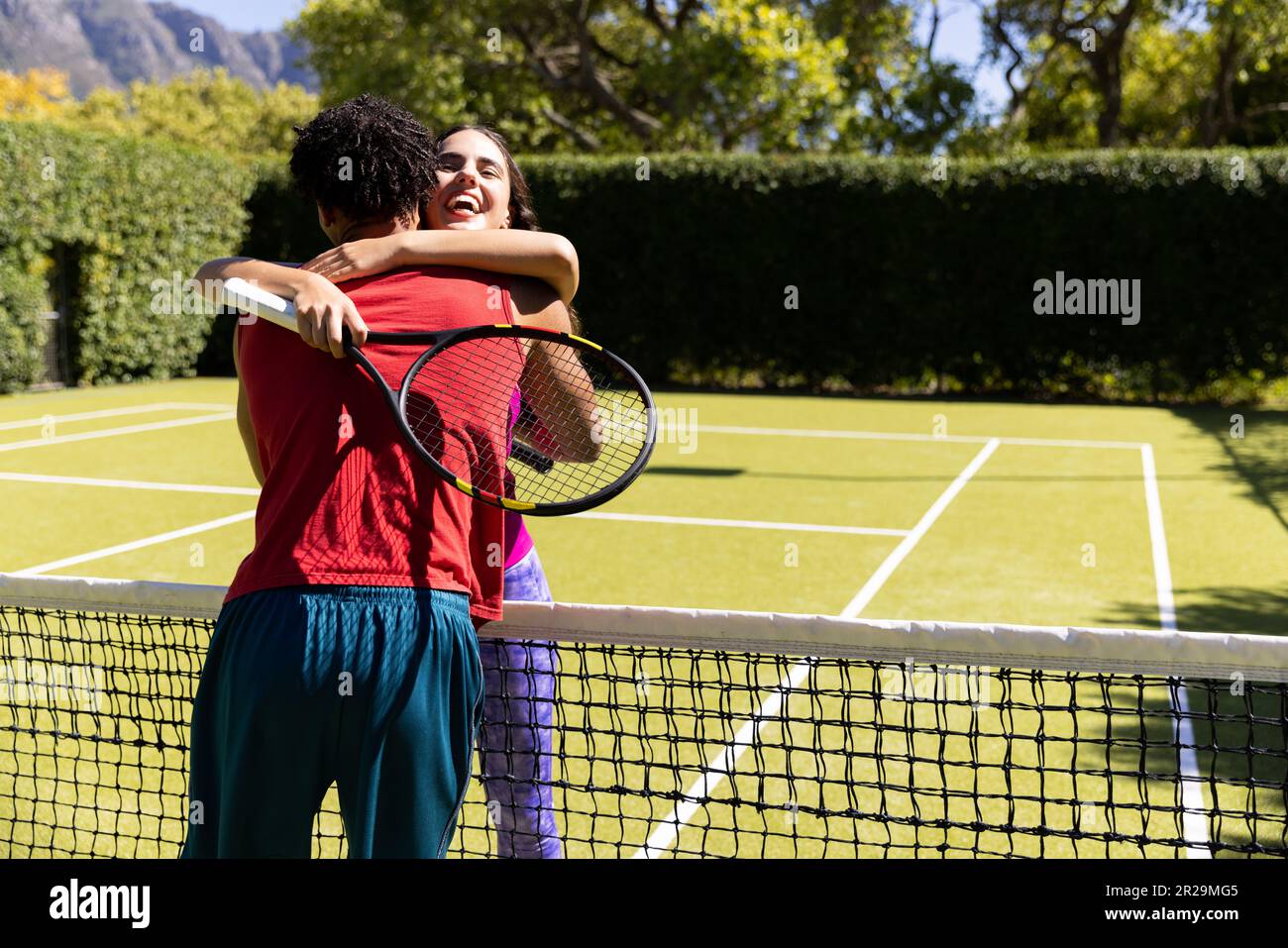Happy Diverse Couple Holding Rackets Embracing Over Net On Sunny