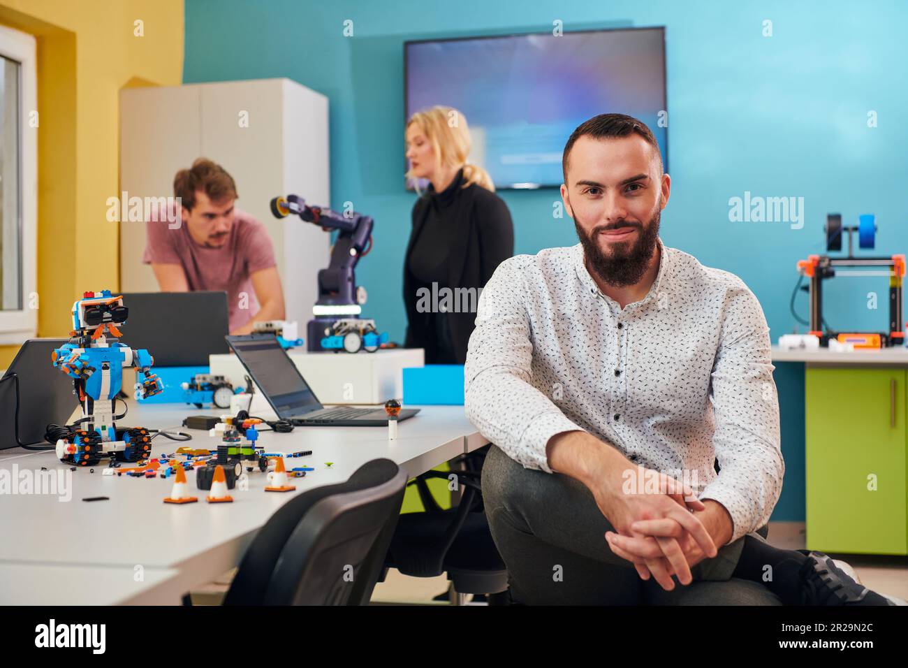 A man sitting in a robotics laboratory while his colleagues in the ...