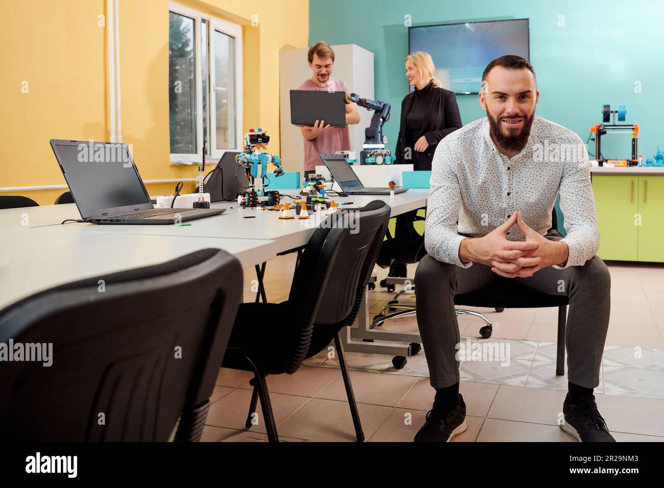A man sitting in a robotics laboratory while his colleagues in the ...