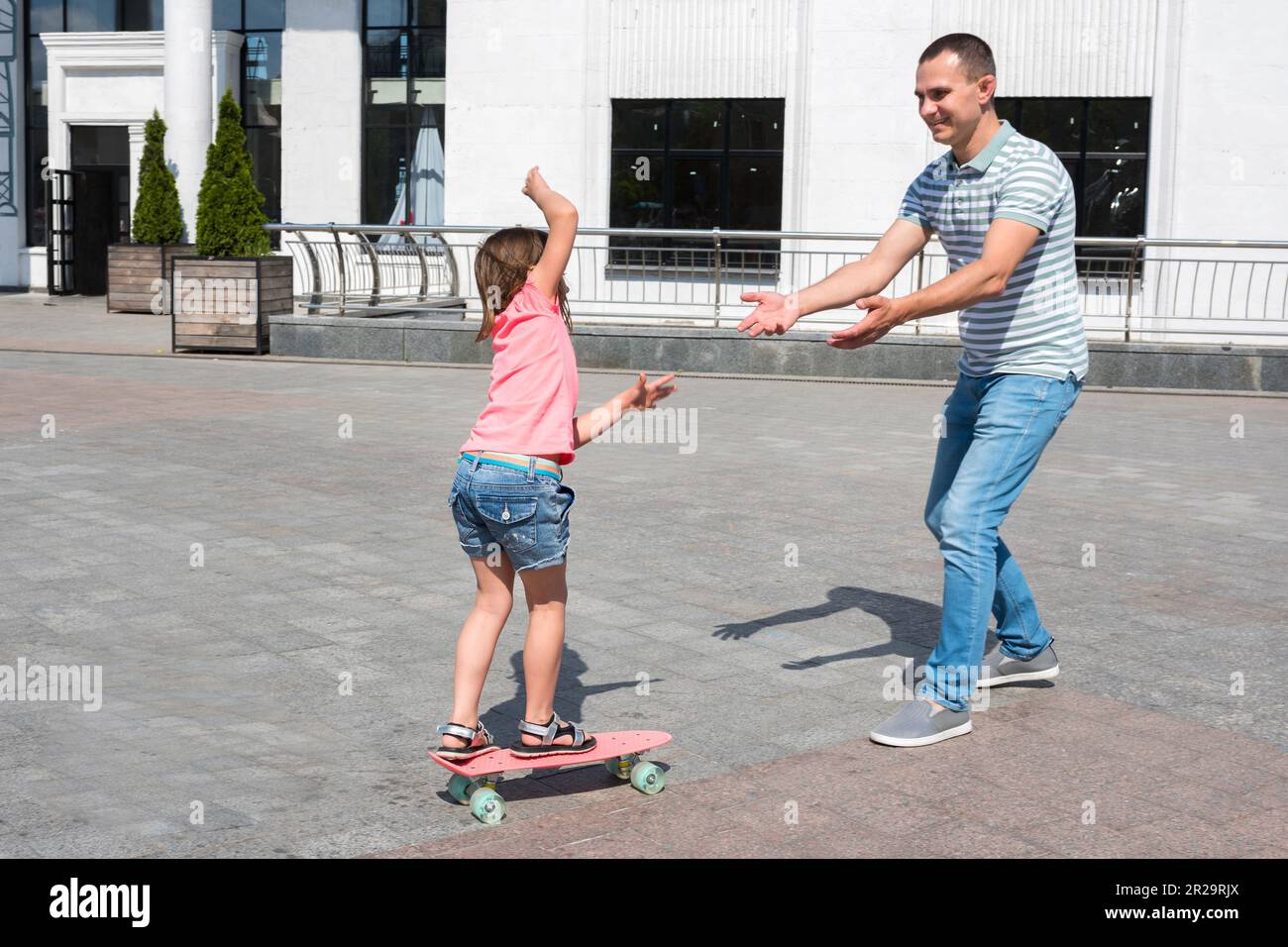 A father is teaching his daughter skateboarding in a city park. A girl ...