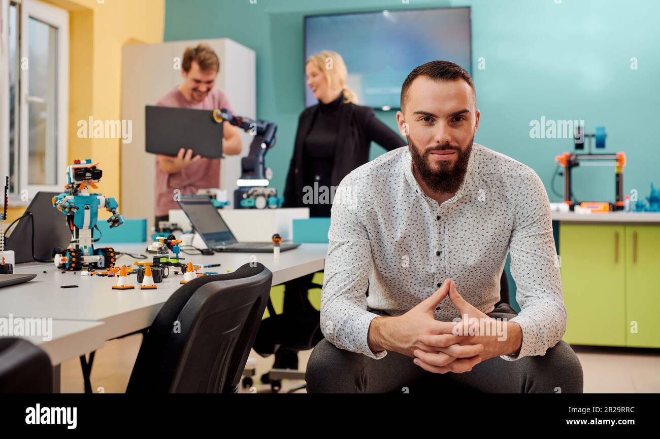 A man sitting in a robotics laboratory while his colleagues in the ...