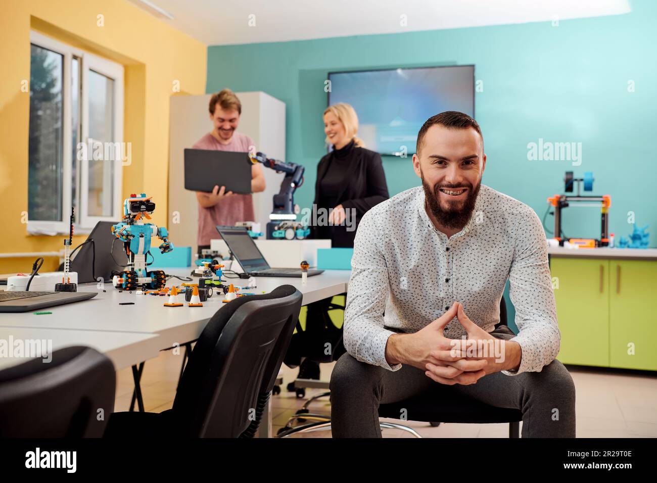 A man sitting in a robotics laboratory while his colleagues in the ...