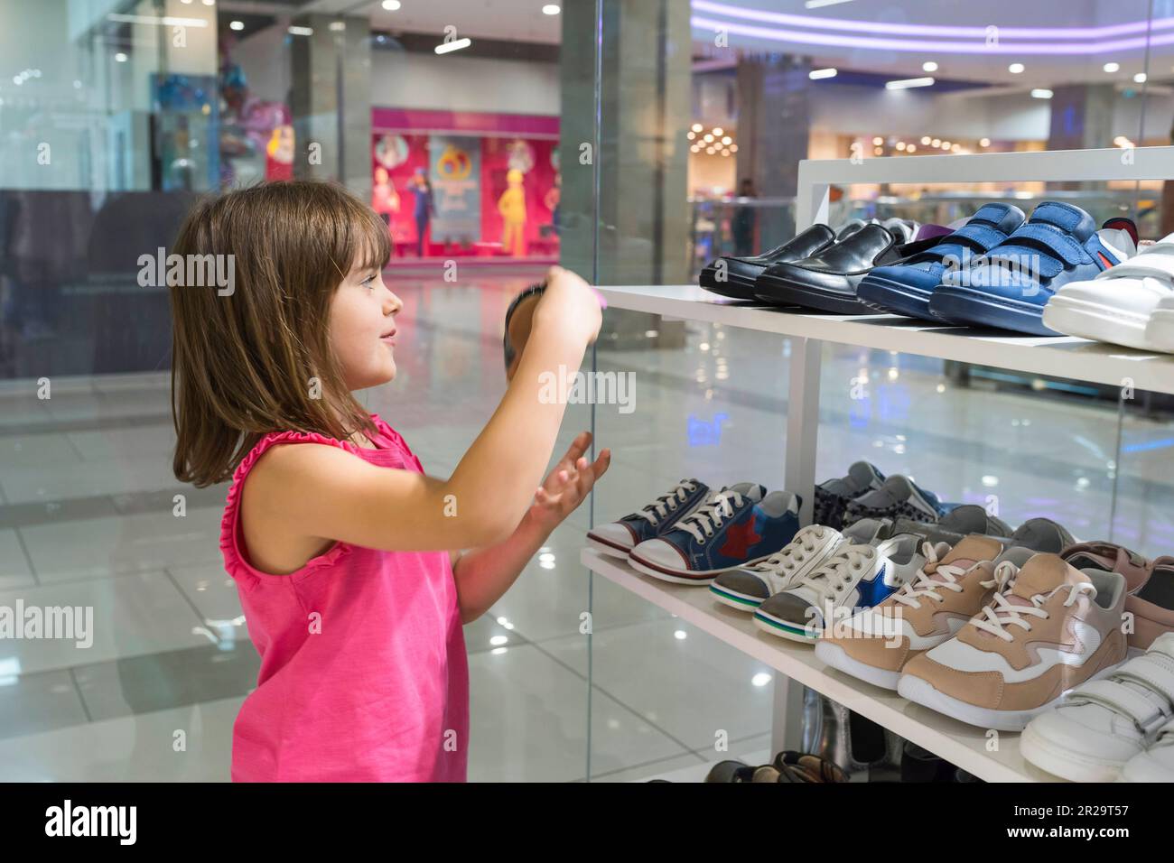 A little girl in a shopping center chooses shoes. Shopping Stock Photo ...