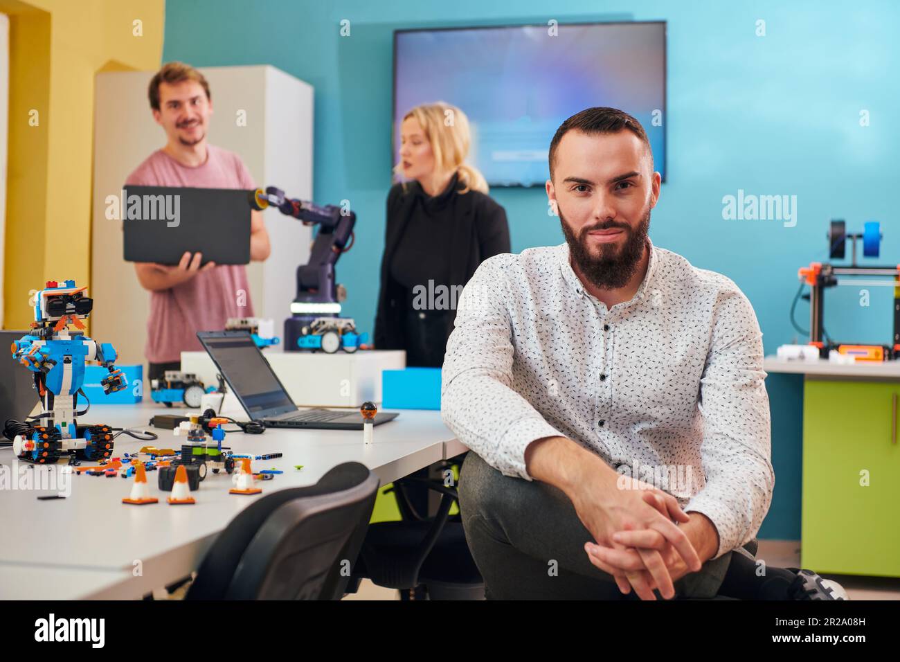 A man sitting in a robotics laboratory while his colleagues in the ...