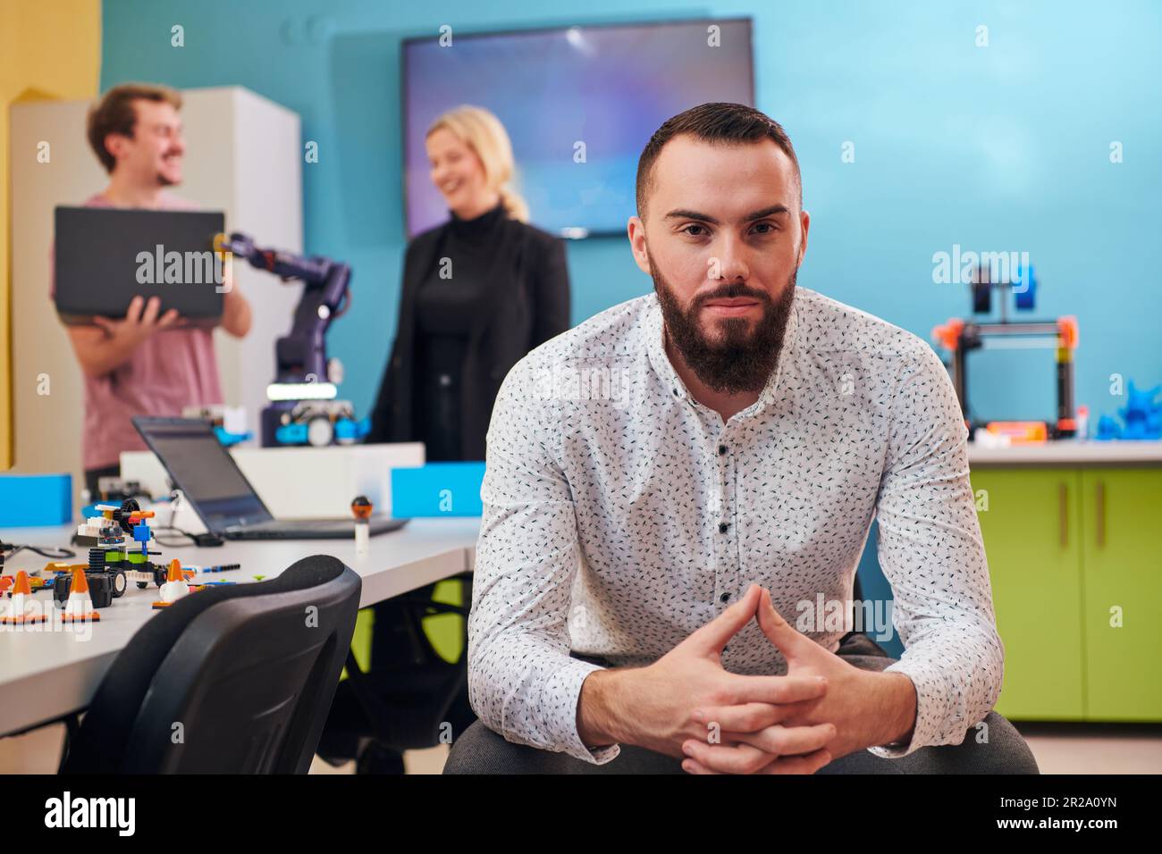 A man sitting in a robotics laboratory while his colleagues in the ...