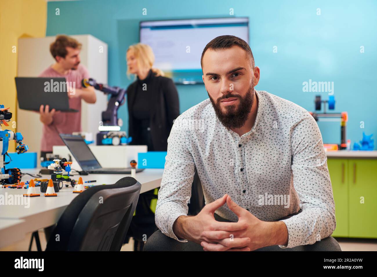 A man sitting in a robotics laboratory while his colleagues in the ...