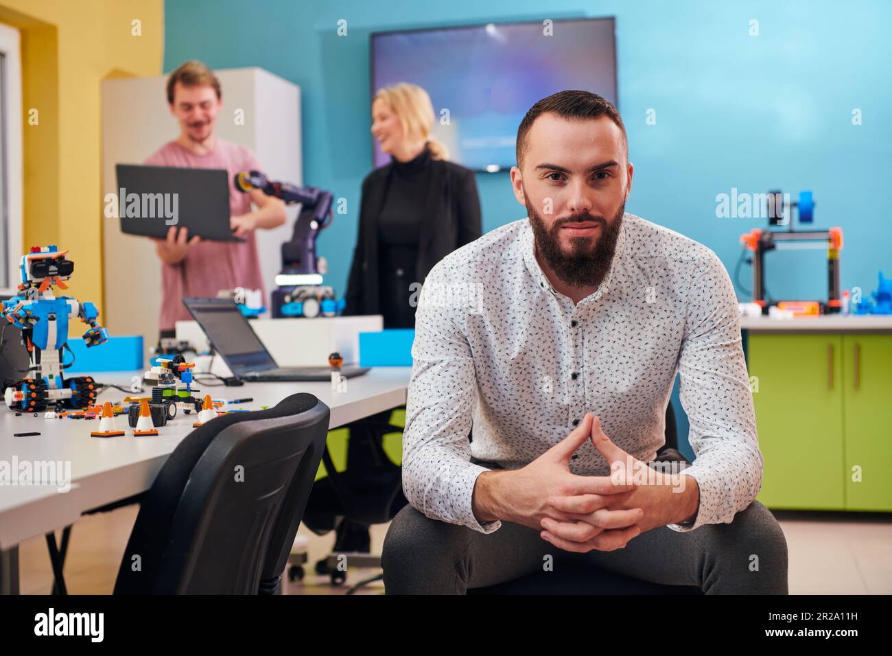 A man sitting in a robotics laboratory while his colleagues in the ...