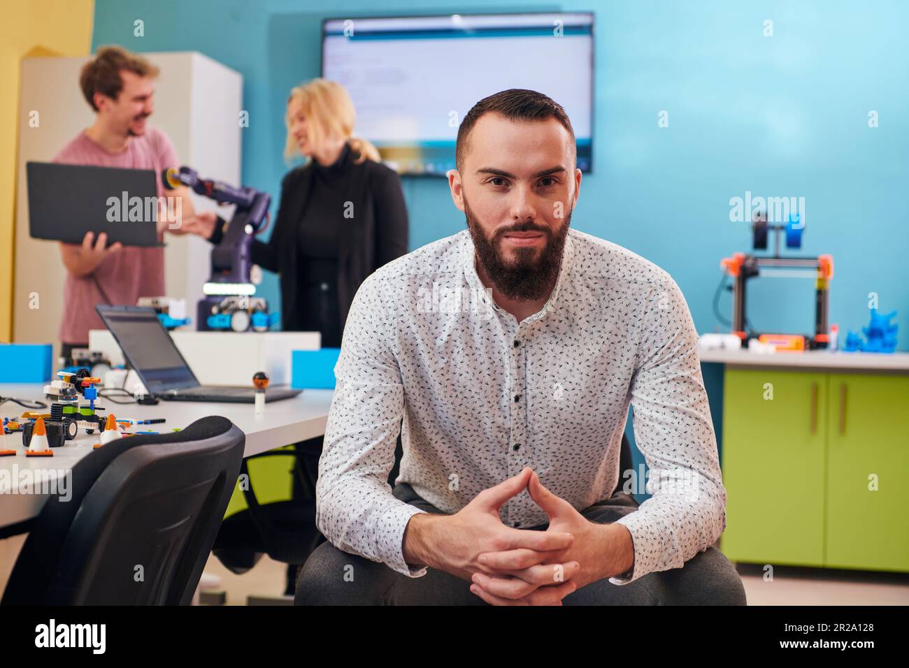 A man sitting in a robotics laboratory while his colleagues in the ...