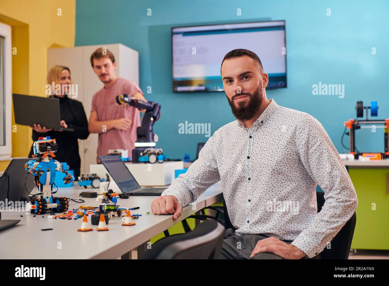 A man sitting in a robotics laboratory while his colleagues in the ...