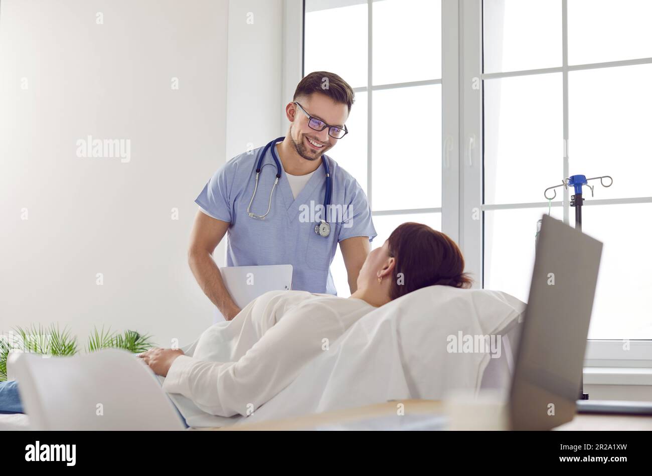 Friendly male nurse gives IV line to woman patient who is lying on medical bed at clinic Stock ...