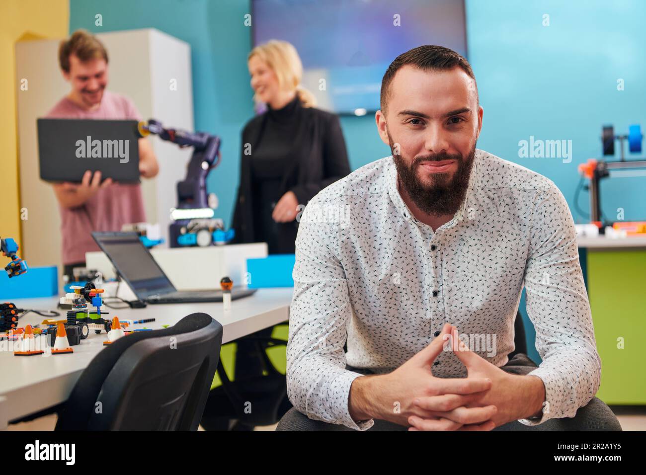 A man sitting in a robotics laboratory while his colleagues in the ...