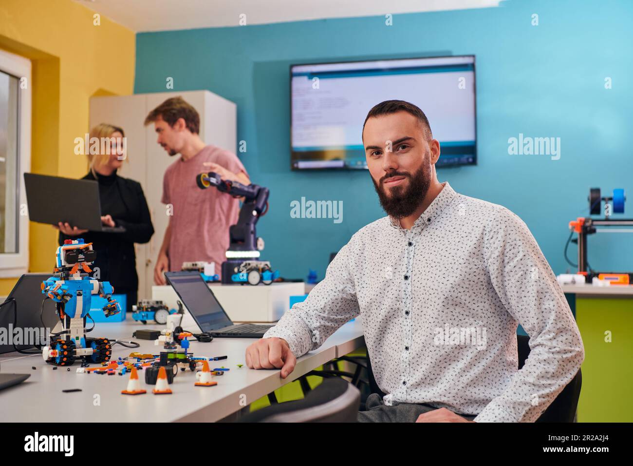 A man sitting in a robotics laboratory while his colleagues in the ...