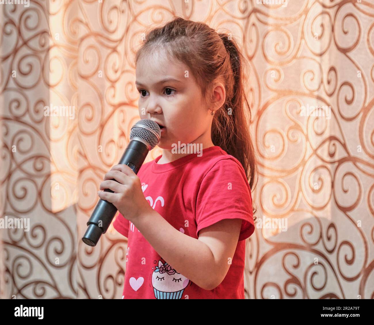 Cute shy little Asian girl holding microphone singing karaoke at home ...