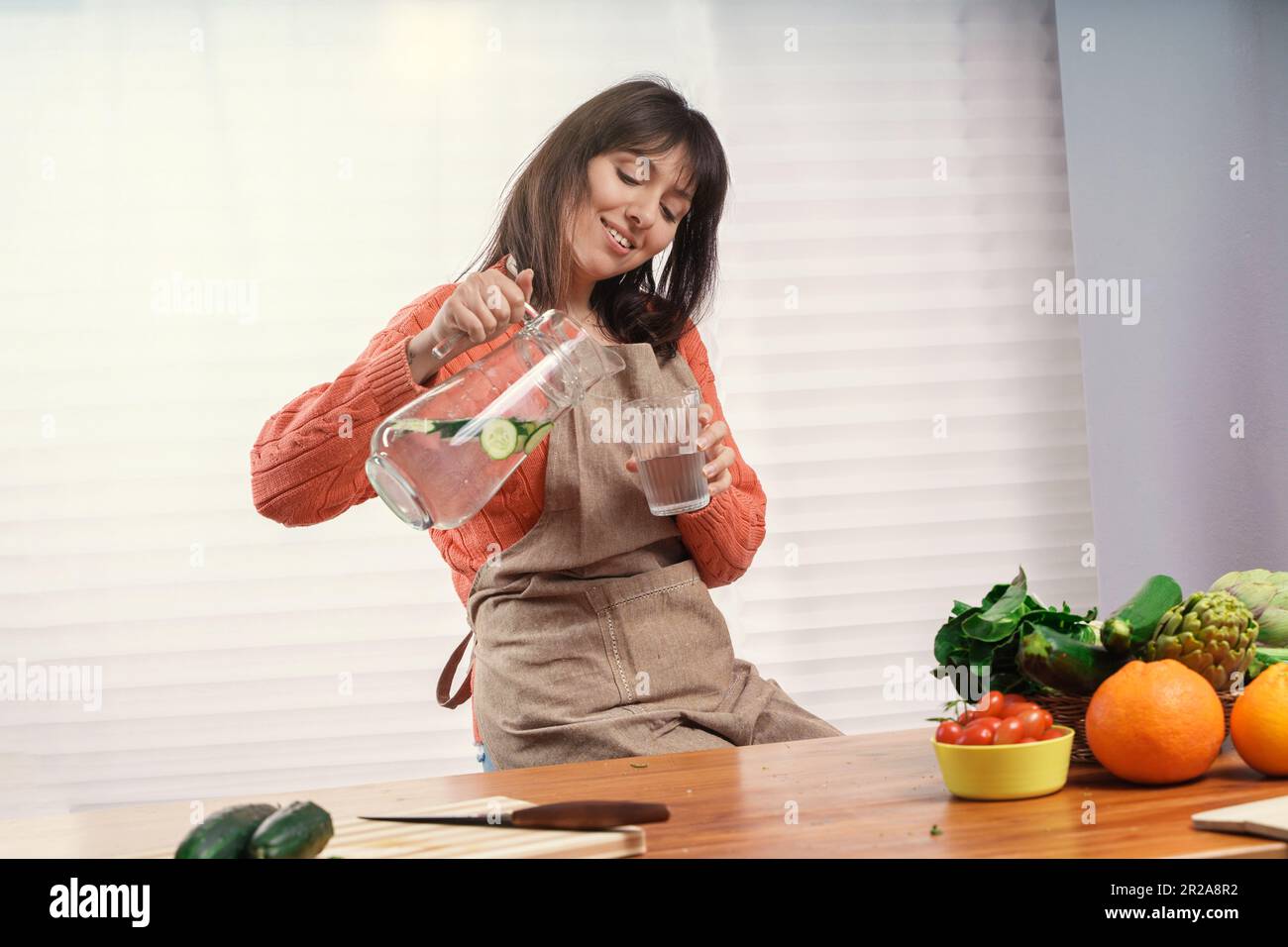 Caucasian woman in a kitchen apron sits at a kitchen table, backlit by ...