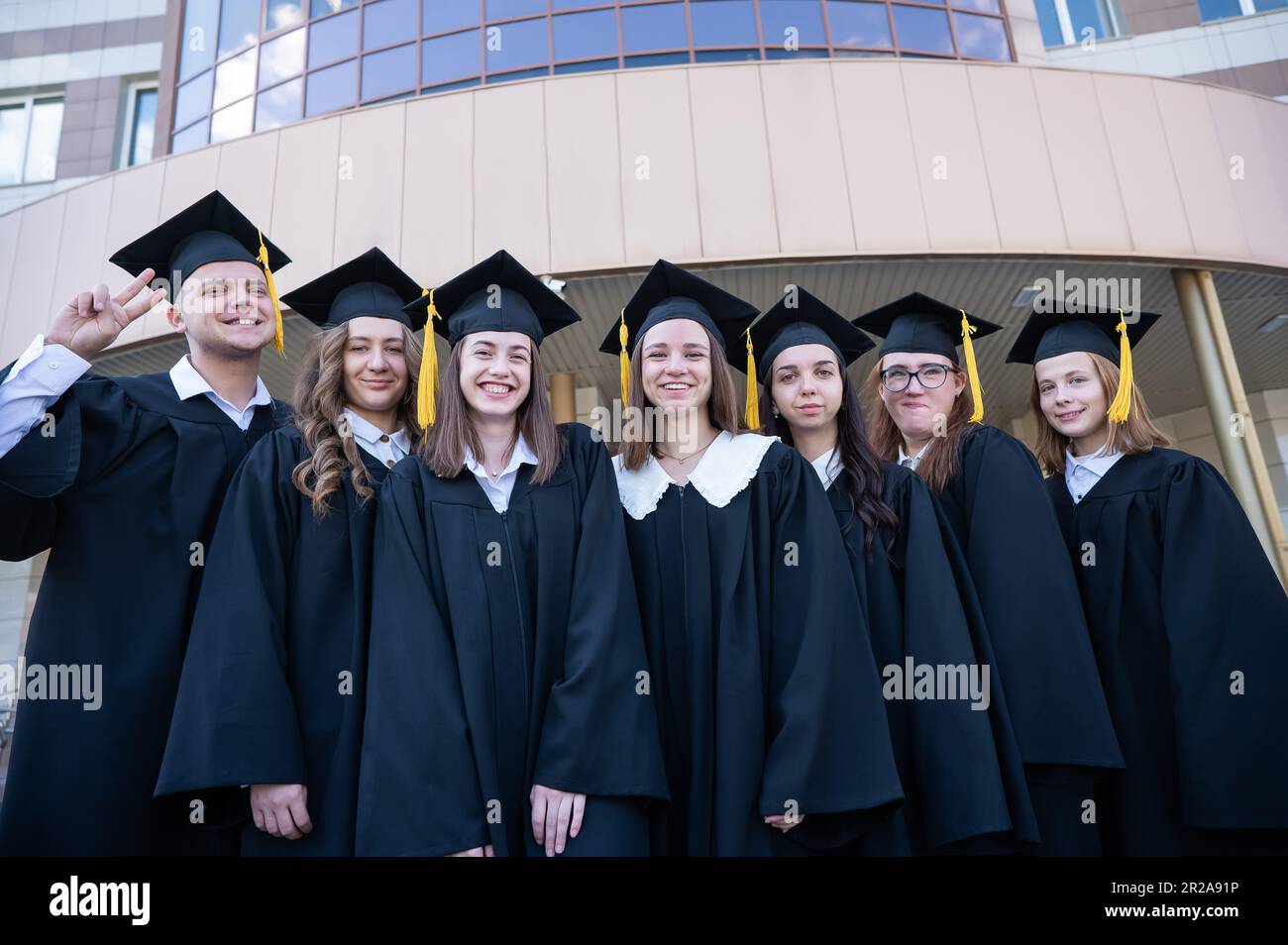 Happy students in graduate gown stand in a row against the backdrop of ...