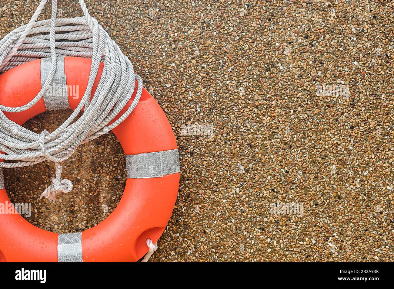 Orange lifebuoy and white rope hanging on gravel wall, copy space for ...