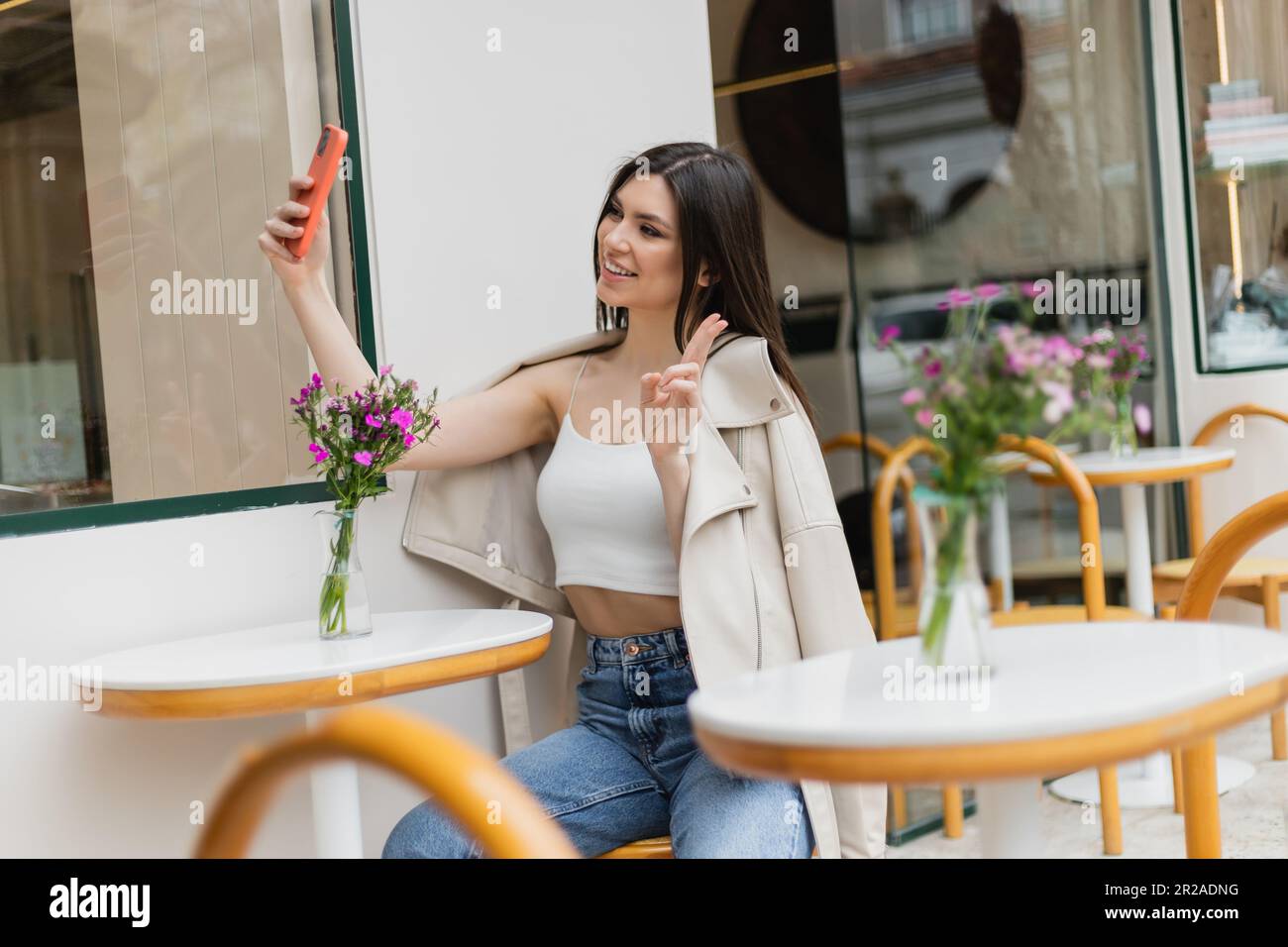happy woman with long hair sitting on chair near bistro table with ...
