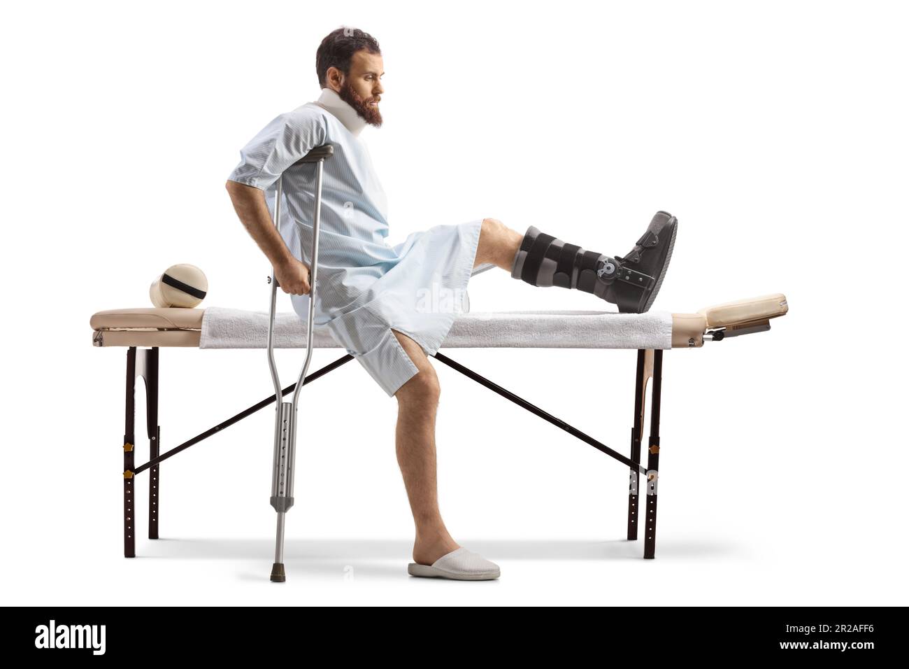 Man in a hospital gown sitting at a medical table with a broken leg and ...