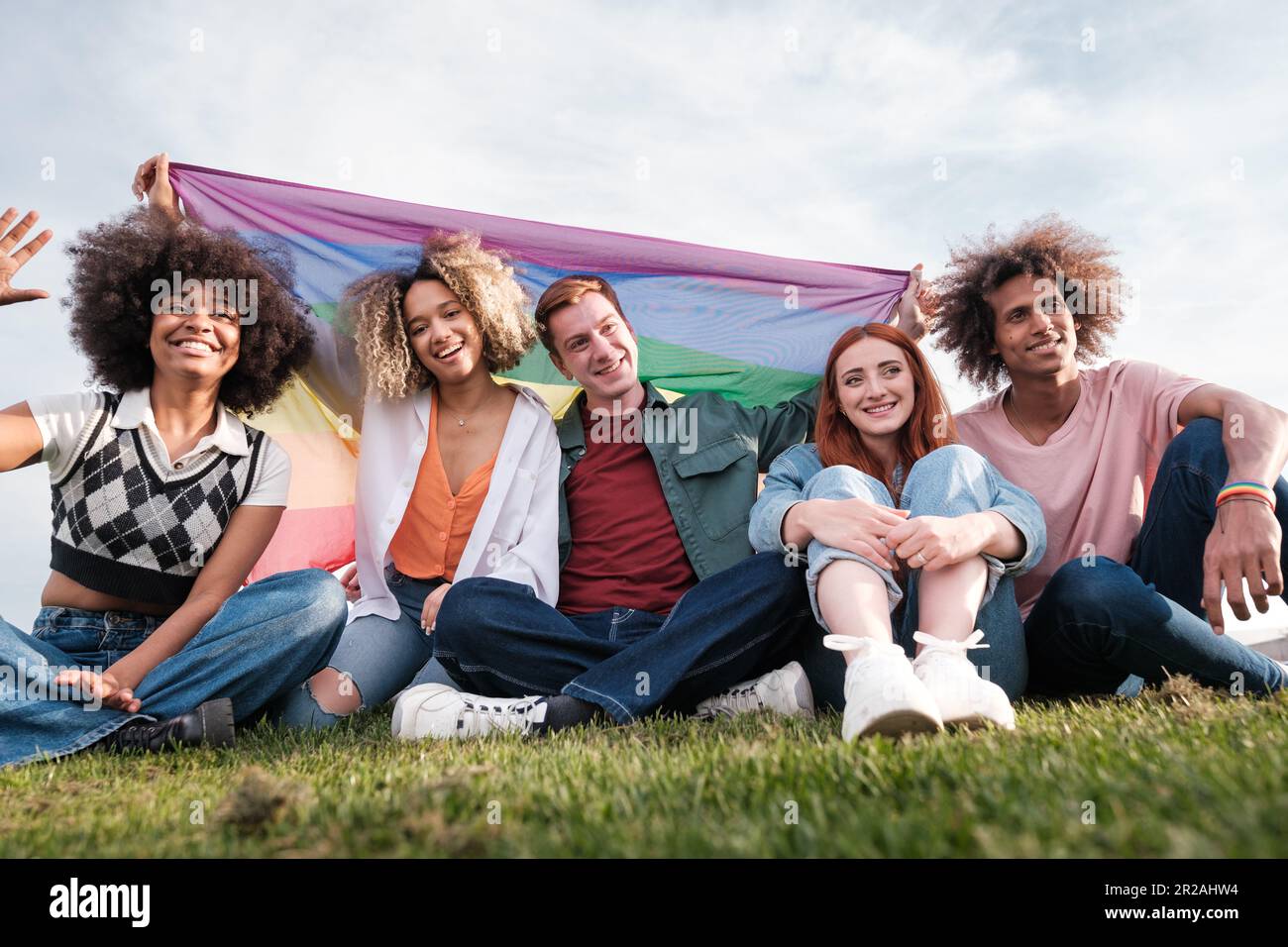 Group of young people sitting on the grass with the gay pride flag ...
