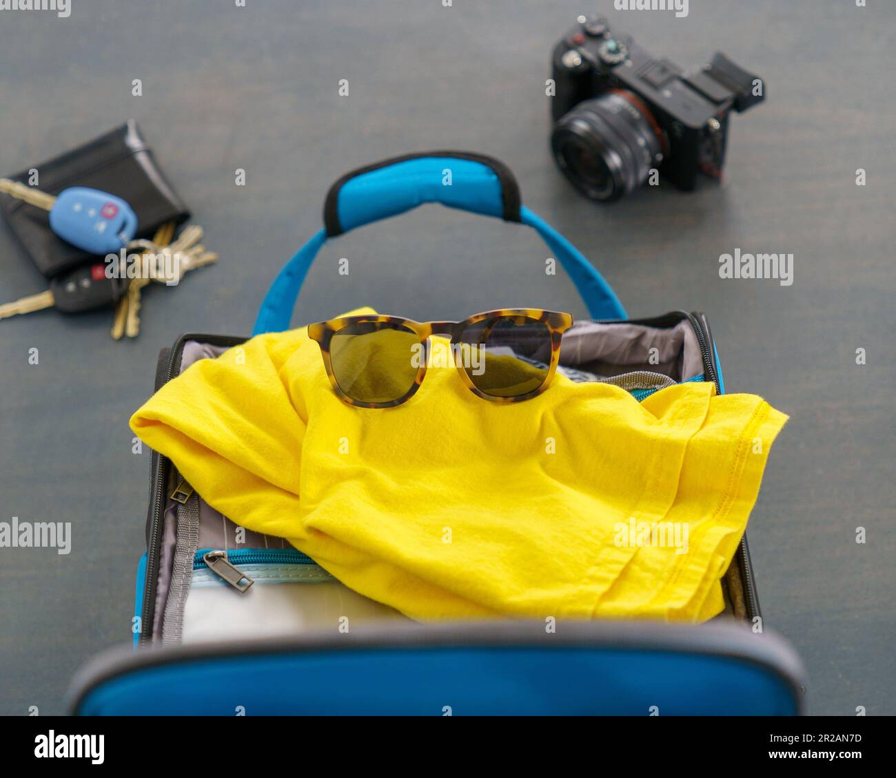 Blue suitcase with a yellow shirt, sunglasses, camera, wallet, and keys ...