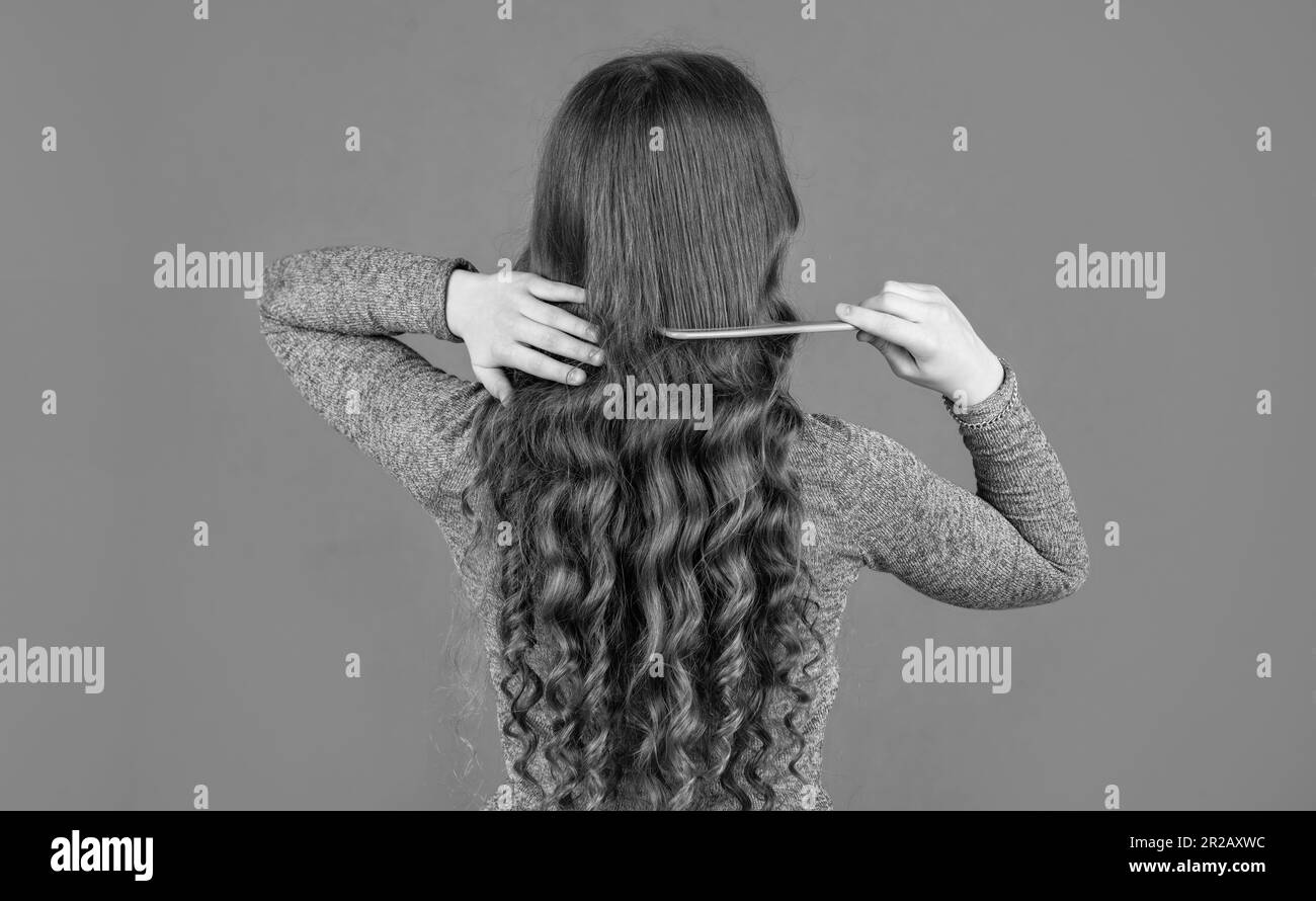 back view of teen girl combing curly hair with hairbrush on pink ...
