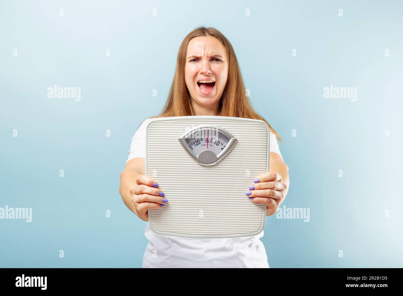 Frustrated young brunette woman in a white t-shirt with weight scale ...
