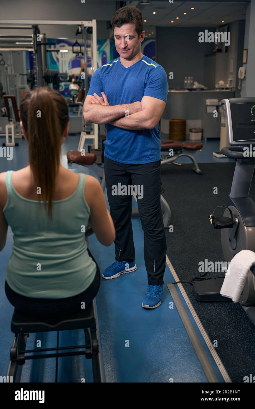 Sporty female working out on fitness equipment supervised by trainer ...