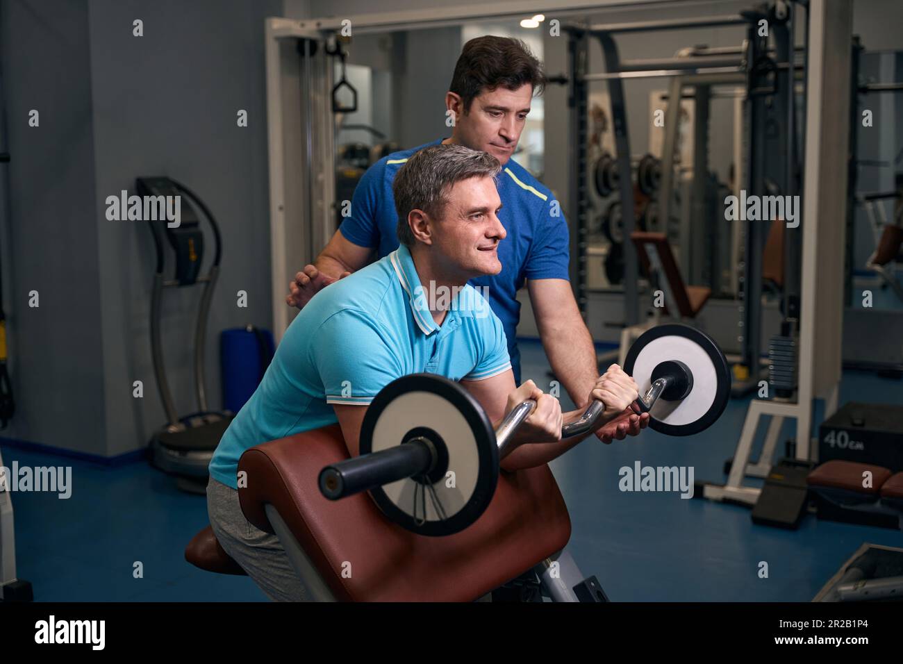 Adult man doing biceps exercise guided by personal trainer Stock Photo ...