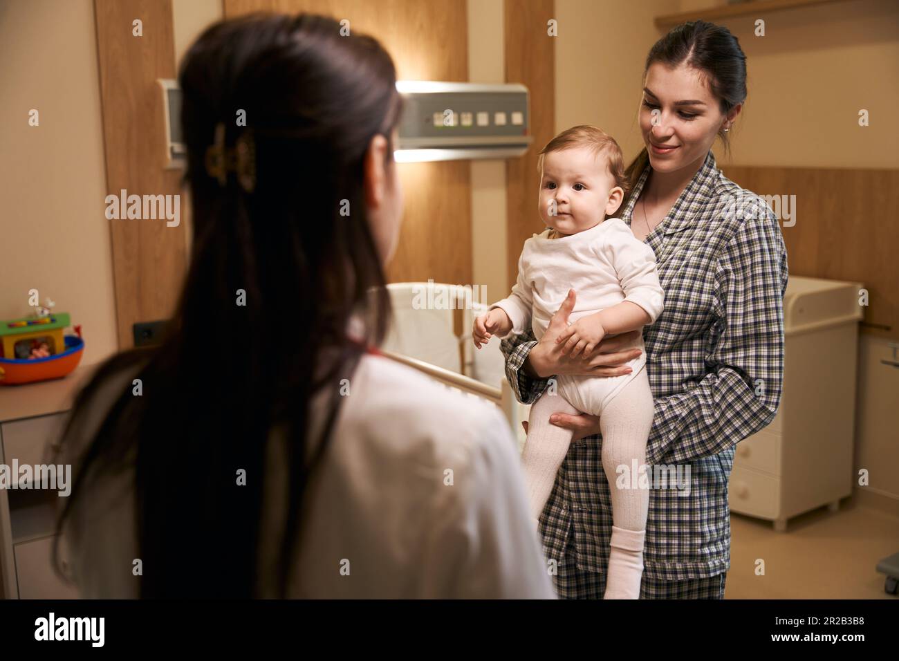 Young mother communicating with attending pediatrician in hospital ward ...