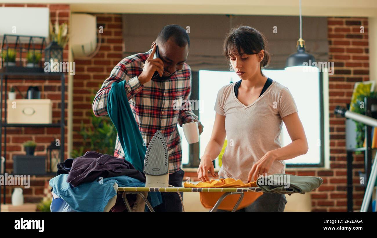 Young housewife ironing laundered clothes and feeling frustrated about ...